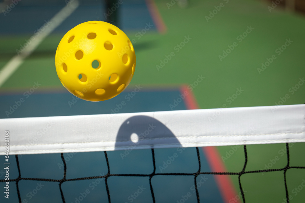 Yellow Pickleball crossing a Pickleball net with shadow on the top tape ...