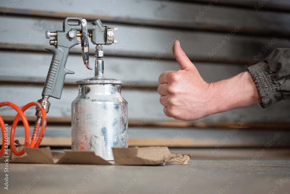 Spray paint gun and painter hand shows a thumbs up gesture close up ...