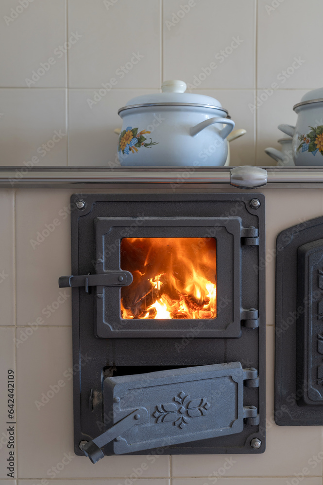 Wood burning tiled stove with fire in the kitchen with white pots on ...