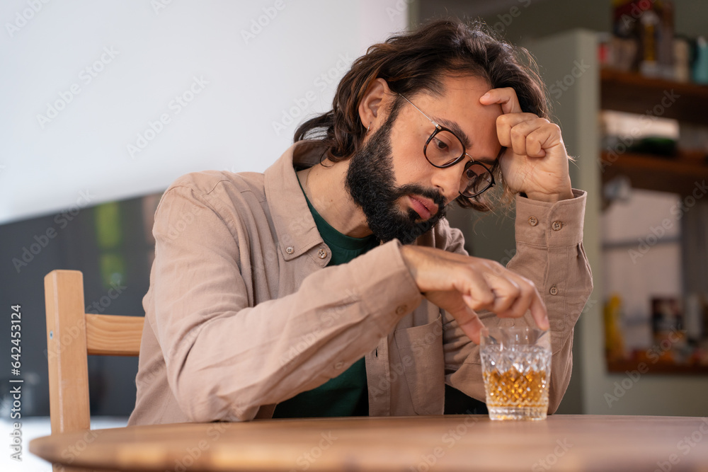Upset young man drinker alcoholic sitting at bar counter with glass drinking whiskey alone, sad ...