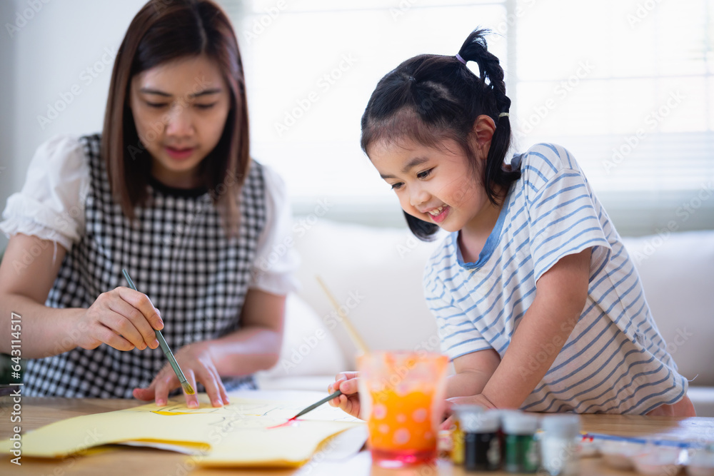 Cute little child painting with colorful paints. Asian girl and mother using crayon drawing ...