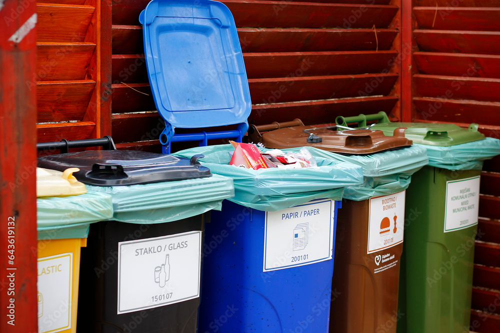 Five colorful recycle plastic bins with description in wooden shelter ...