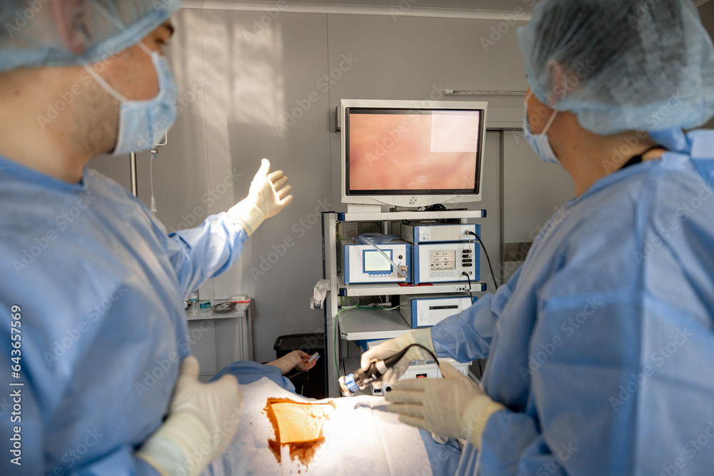 Two surgeons performs minimally invasive procedure with endoscopes, looking on monitor in ...