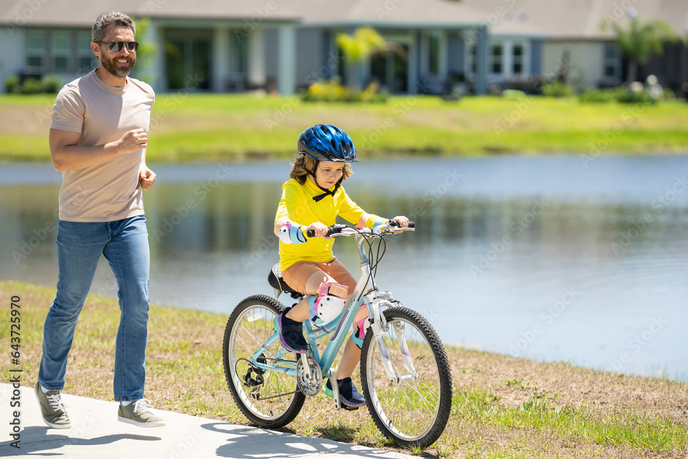 Father and son riding bike on a park. Child in safety helmet with father riding bike on summer ...