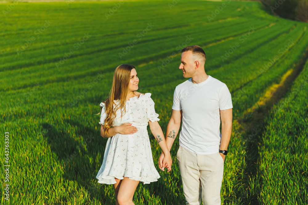 Pregnant couple hugging in a green spring field. Expectant parents in ...