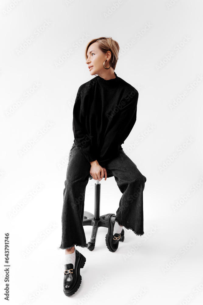 Full body of a woman dressed in a simple black outfit. She sits on a ...