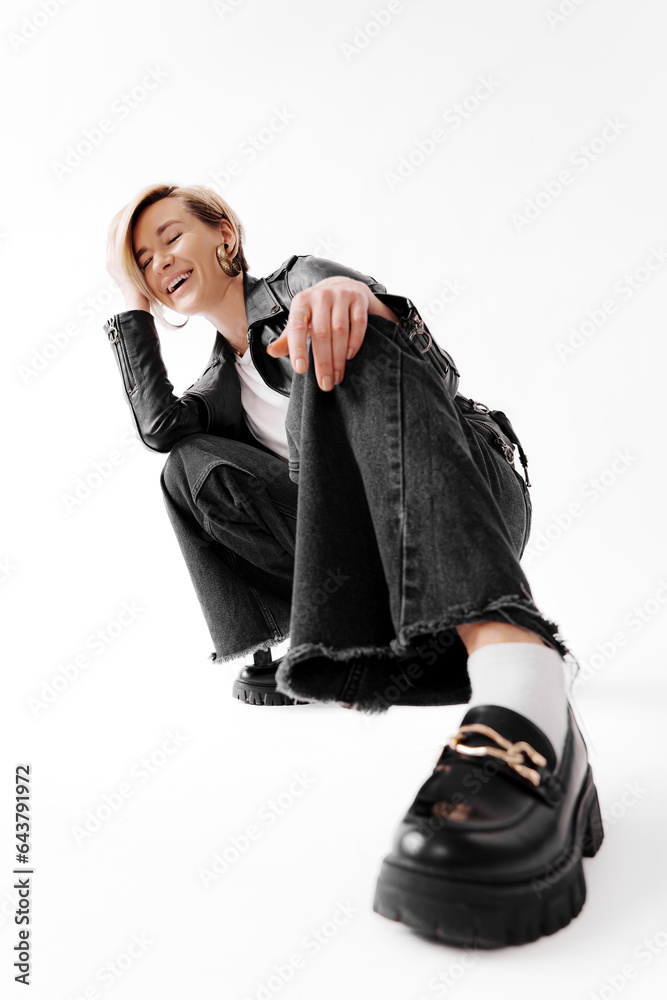 Full body of young female in leather jacket and boots sitting on ...