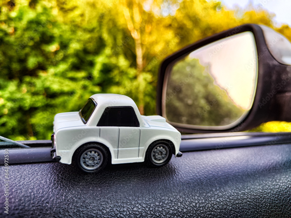 Small white toy car on background of side mirror of a real big caron ...