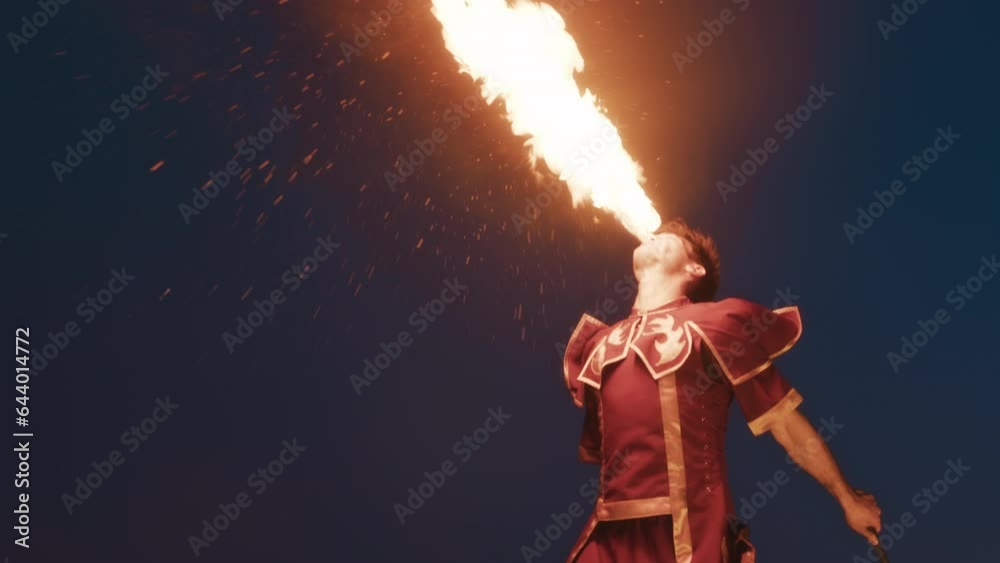 Low angle medium shot of extreme young man breathing and blowing fire ...