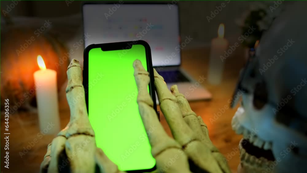 Skeleton stroking the green screen of smartphone with creepy bone ...