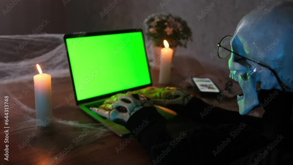Skeleton bony hands typing at laptop keyboard with chromakey in screen ...