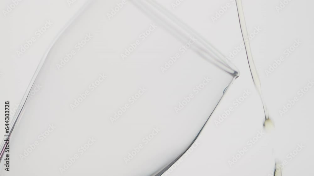 Beer is poured into a tilted glass on a light white background in slow ...