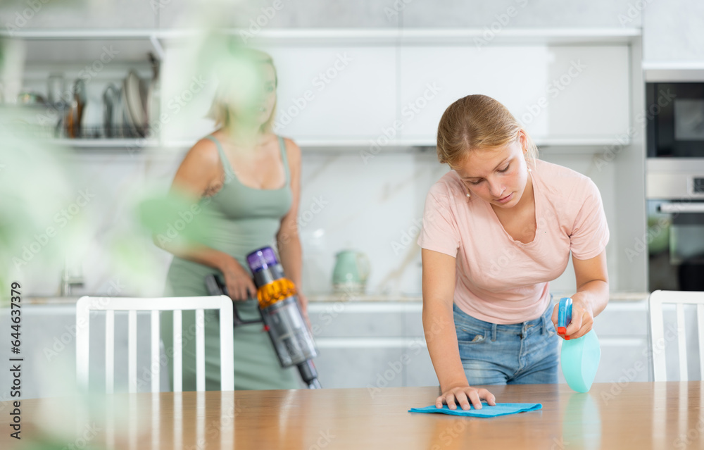 Foto de Positive teenage girl wiping table with rag and detergent at ...