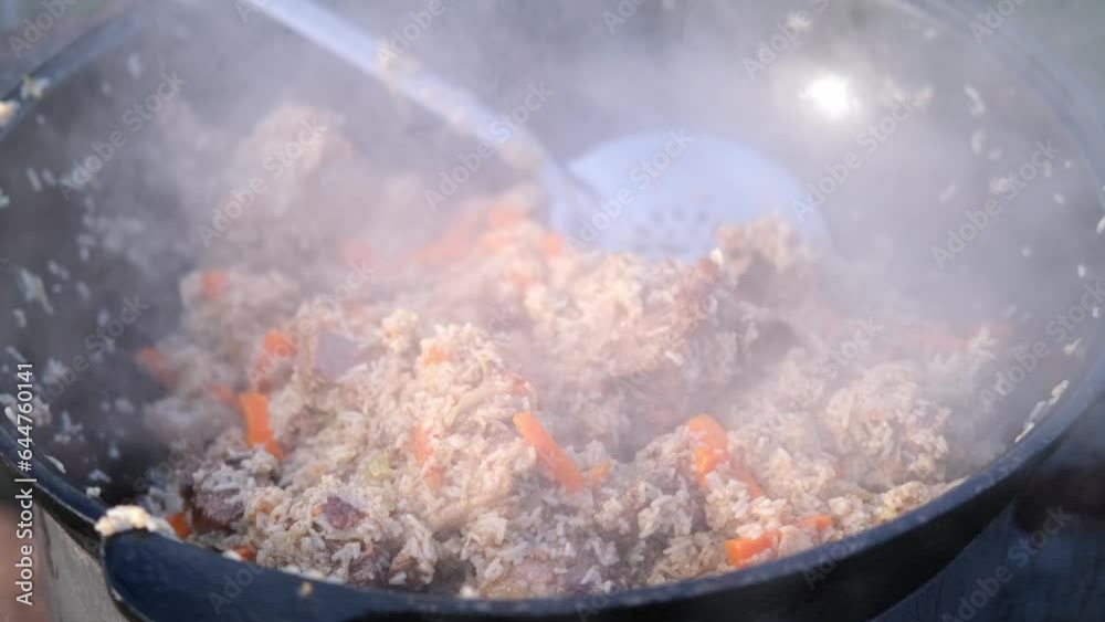 Cooking traditional pilaf in a cauldron in nature, outdoors. Eastern ...