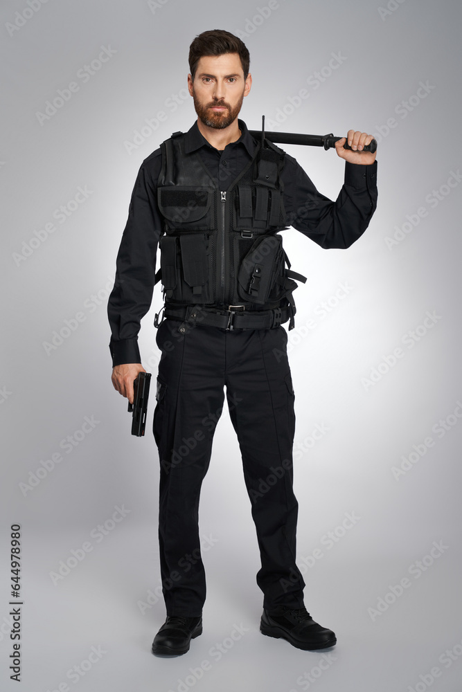 Serious dark-haired police officer posing, with baton on shoulder ...