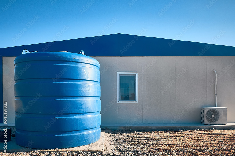 Blue plastic water tank stands next to prefabricated industrial ...