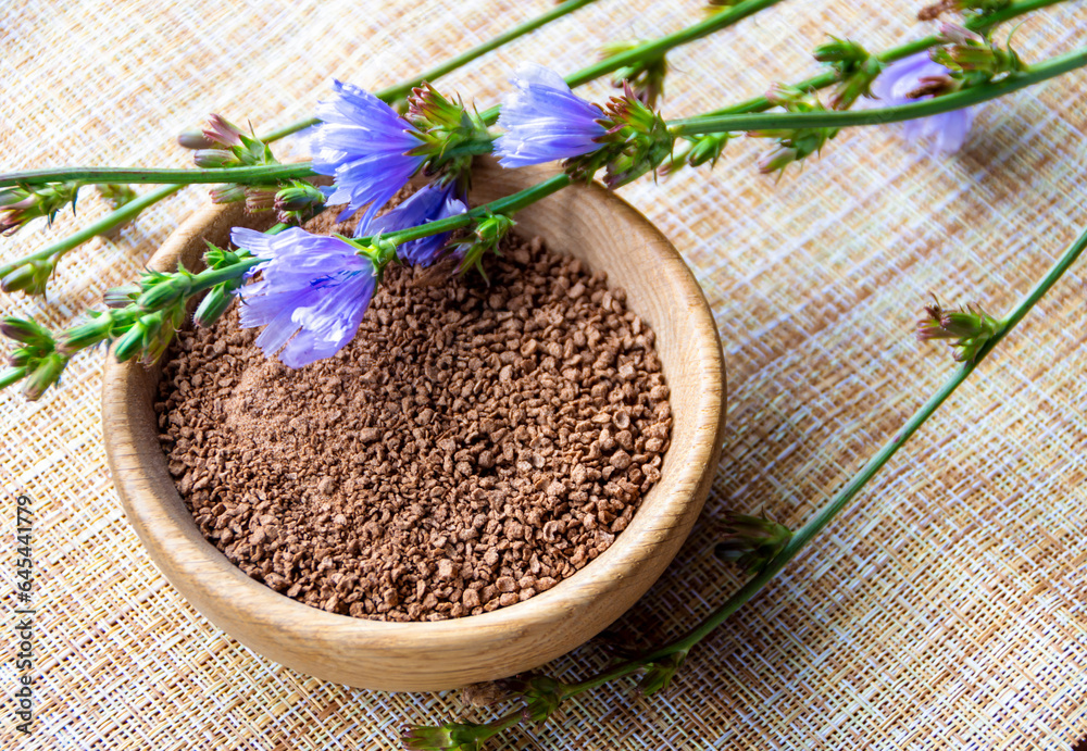 Ground chicory root in a wooden cup and chicory flowers on a rustic ...