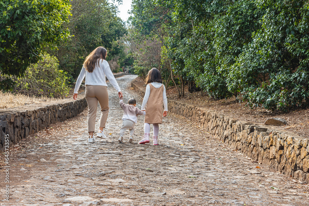 Mother walking with her children along a path, holding hands. Mom is ...