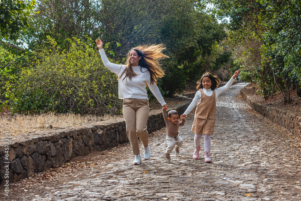 Mom running with her children holding hands, on an autumn trail ...