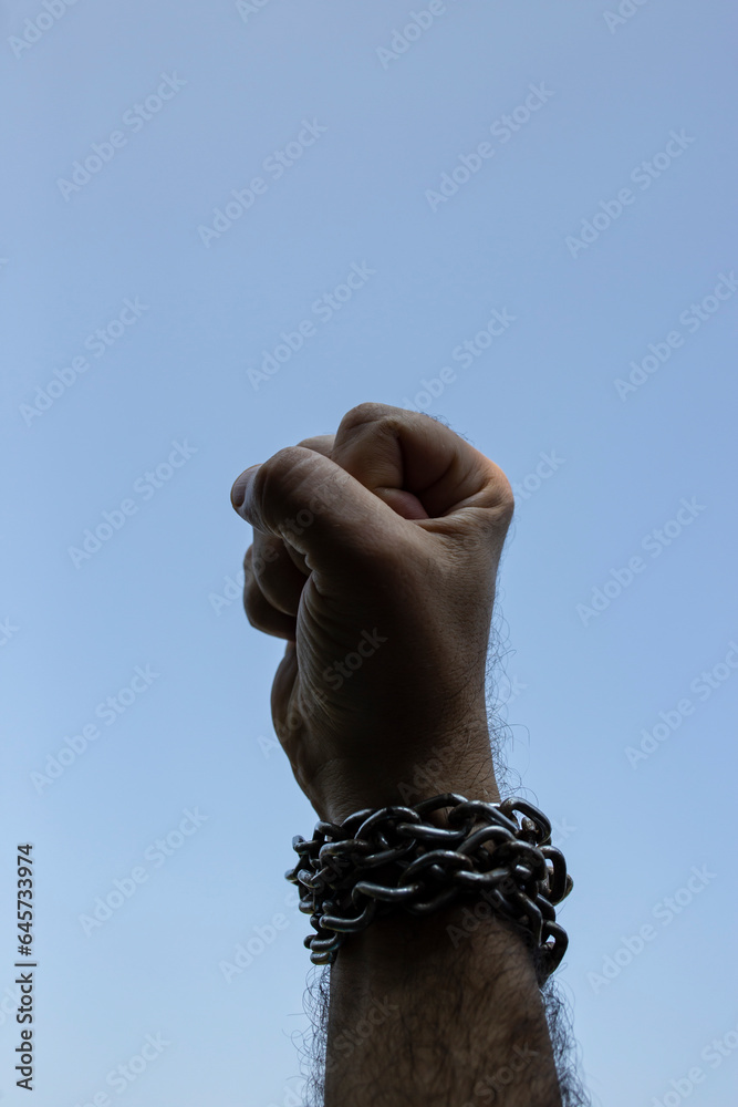 Clenched male fist raised with steel chain tied on the wrist, against ...