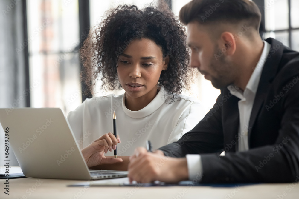 Focused multiracial colleagues sit at desk in office look at laptop ...