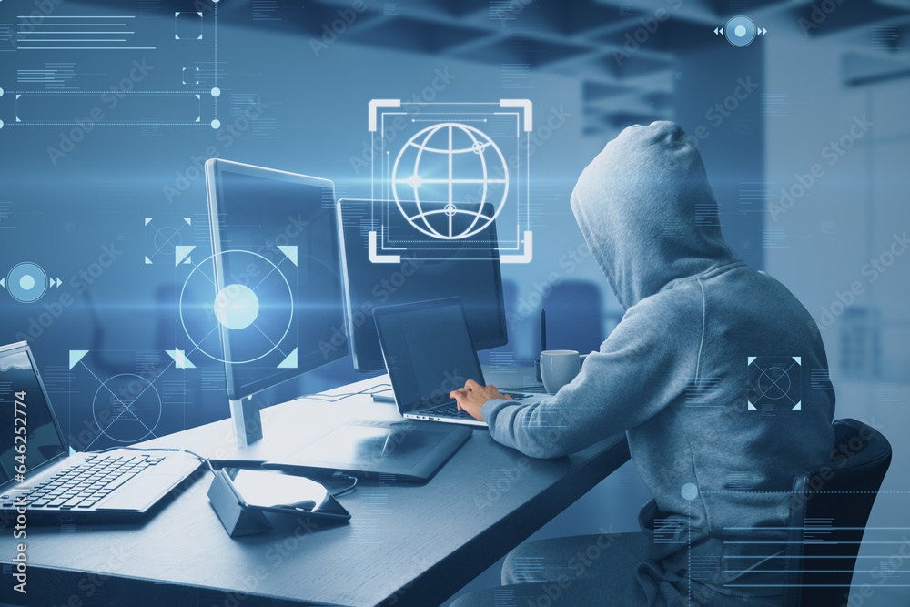 Side view of hacker at desk using computers with creative hacking interface on blurry interior ...