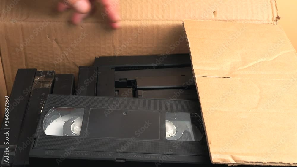 Old VHS tapes in a cardboard box. A man opens a cardboard box with VHS ...