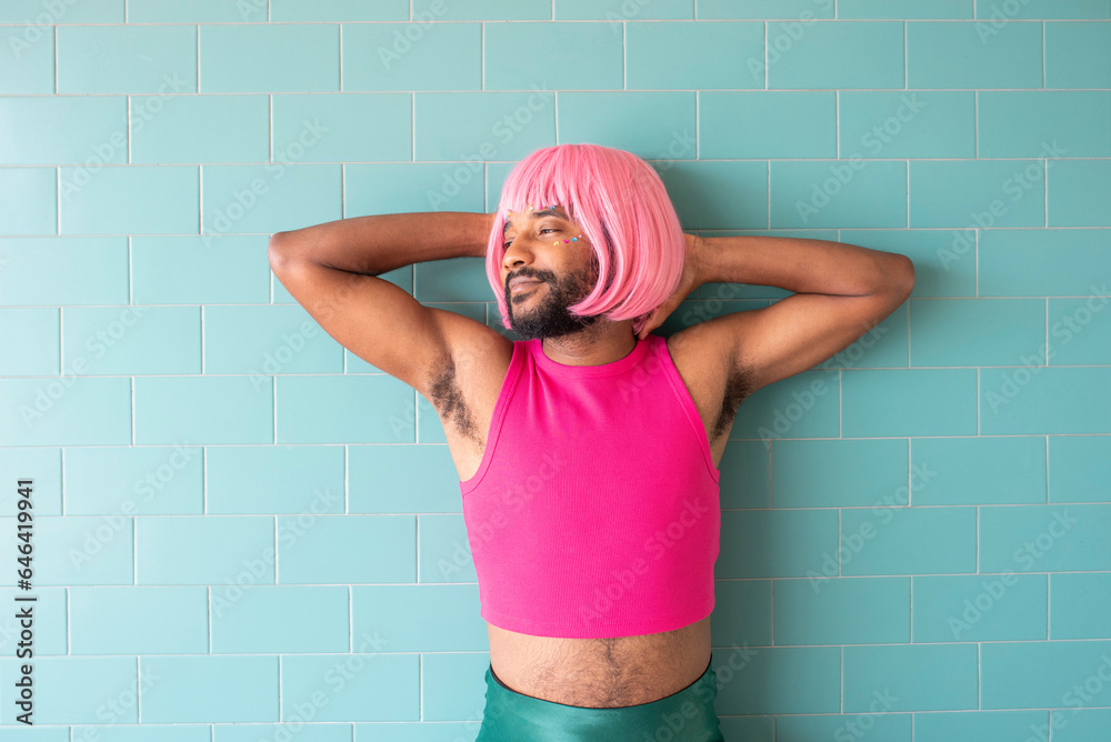 Young queer man with hands behind head in front of tiled wall Stock ...
