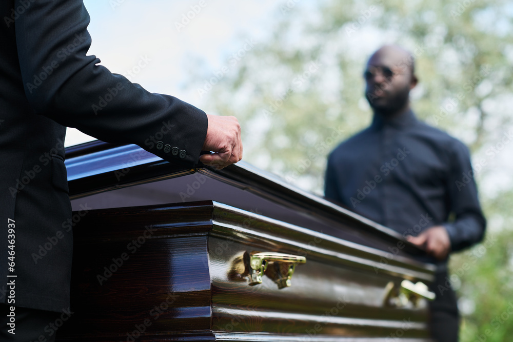 Two intercultural men in black attire closing coffin lid after farewell ...
