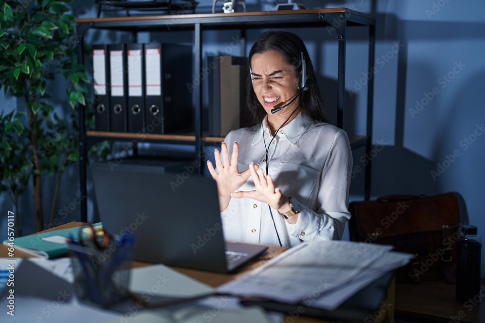 Young brunette woman wearing call center agent headset working late at ...