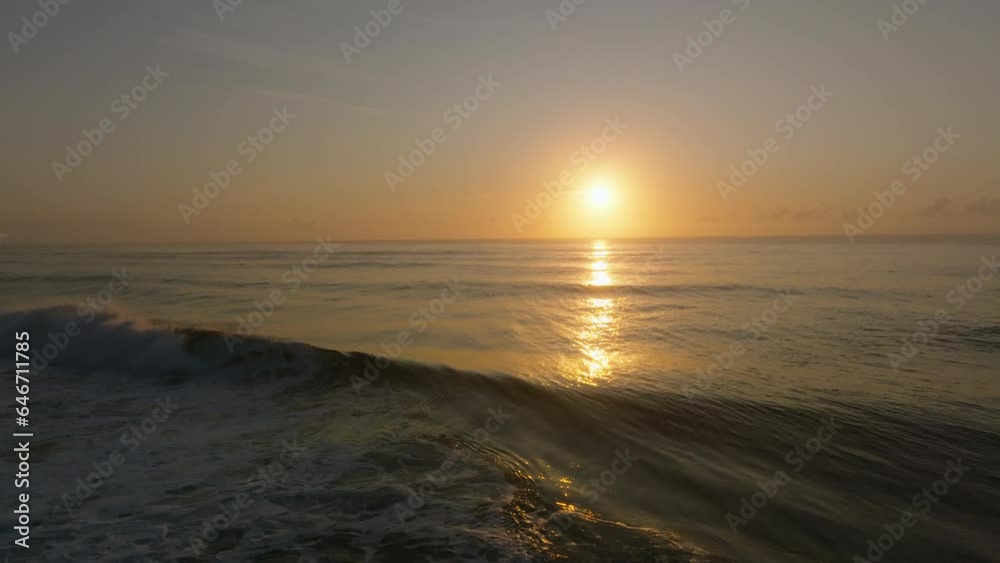 Backwards slowmo shot of ocean wave breaking against sunset backdrop in ...