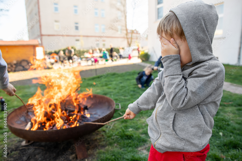 Cute little adorable baby boy put big wooden stick in fire pit with ...