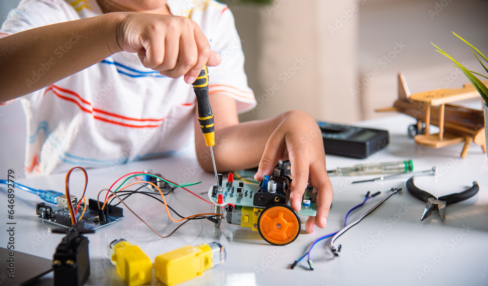 Asian kid boy assembling the Arduino robot car homework project at home, Little child tighten ...