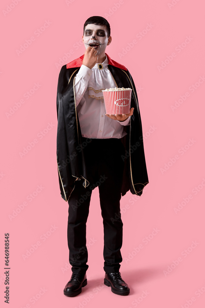 Young man dressed for Halloween as vampire eating popcorn on pink ...