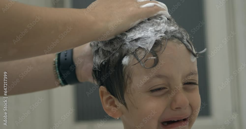 Child crying while mother's hand scrubs his hair with shampoo ...