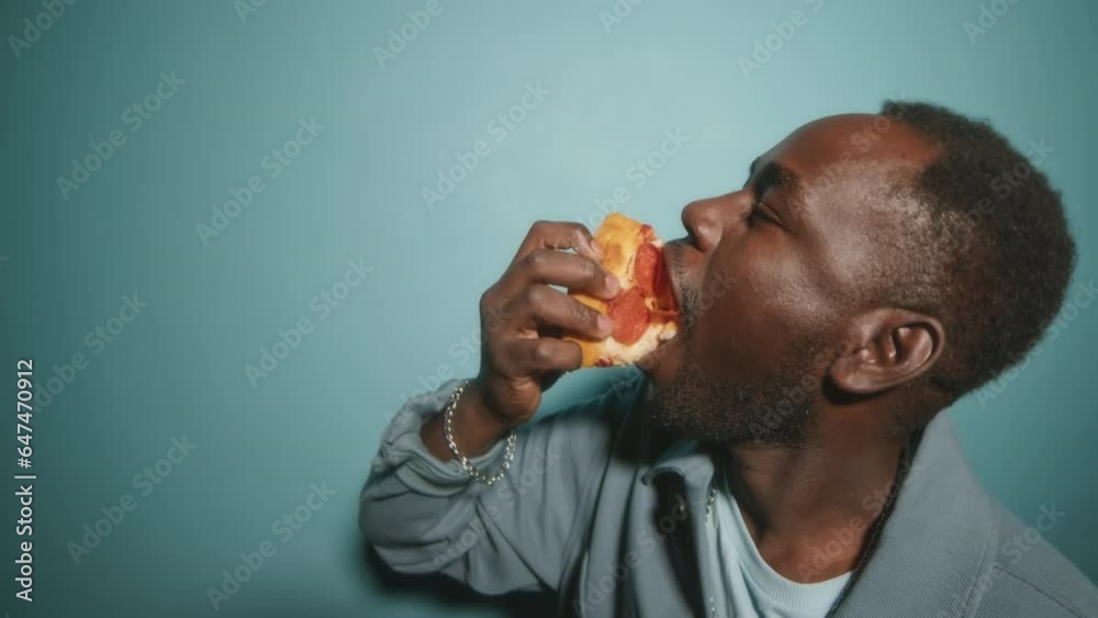 Side view chest up of hungry African American guy eating pepperoni ...