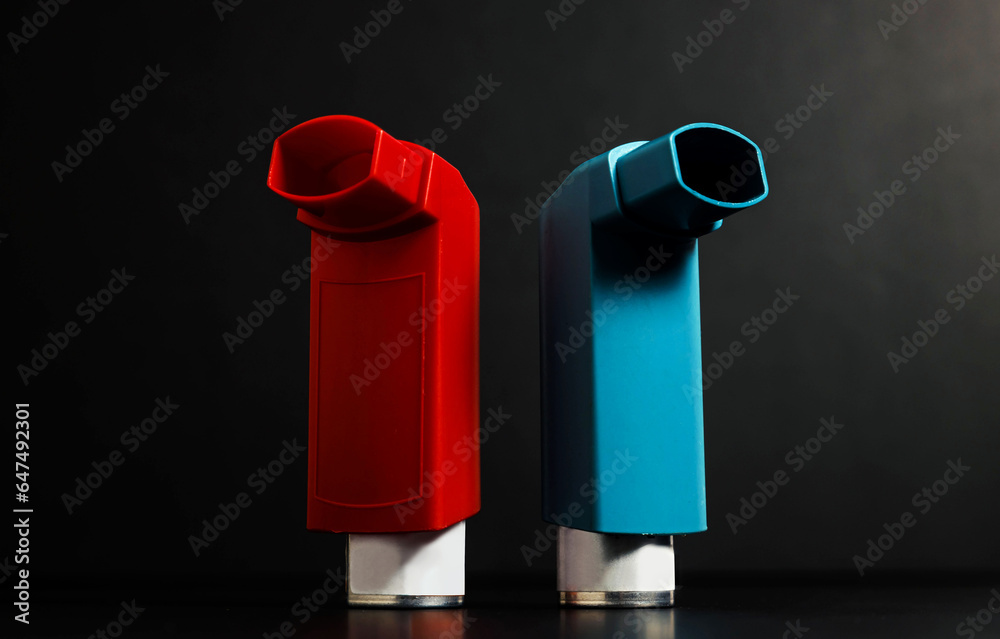 Two asthma inhalers, in red and blue, isolated on a dark background ...