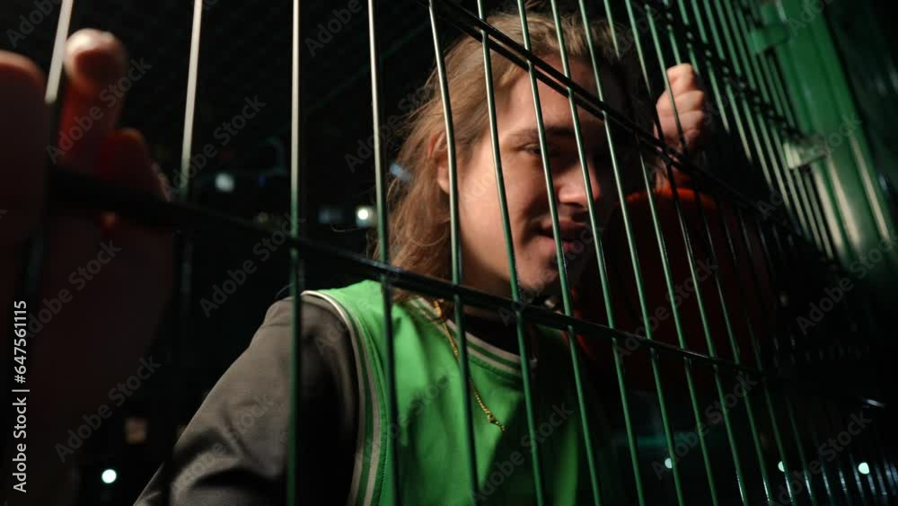 Young smiling man standing behind mesh fence on sports ground looking ...