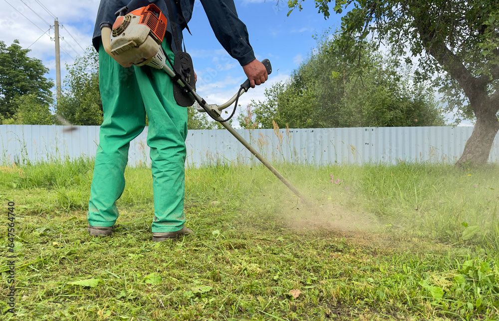 Gardener mows weeds grass. Man cutting grass in yard by using string ...