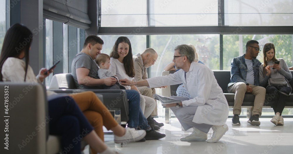 Diverse people sit on couches in clinic lobby area, wait for doctors ...