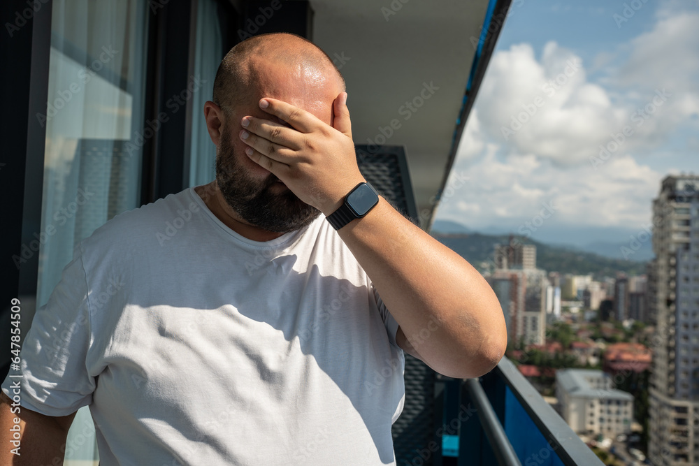 Overweight man hiding from sun covering face with hand standing on ...