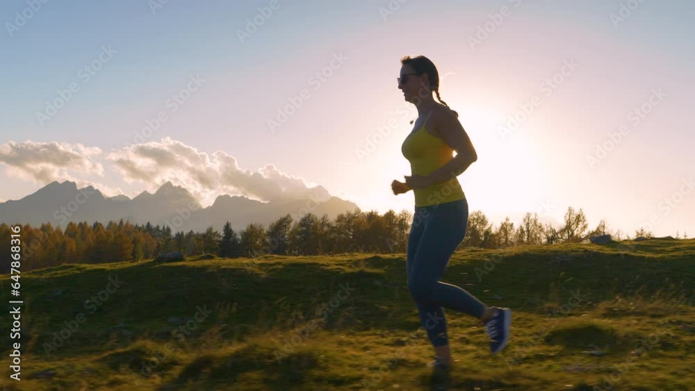 CLOSE UP, LENS FLARE: Female runner jogging in sunset light along a ...