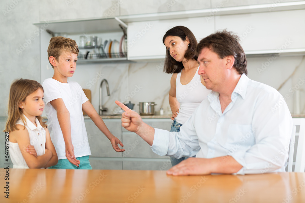 Little brother and sister standing in the kitchen being admonished by ...