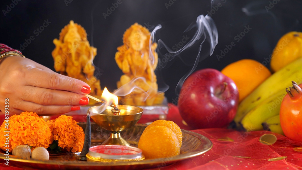 Woman lighting a brass Diya kept on a religious Pooja Thali for Ganesh ...