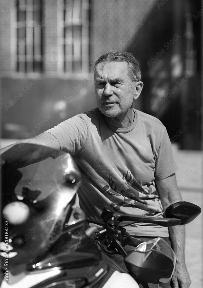 Portrait of a man pushing his motorcycle, looking at viewer, black and ...