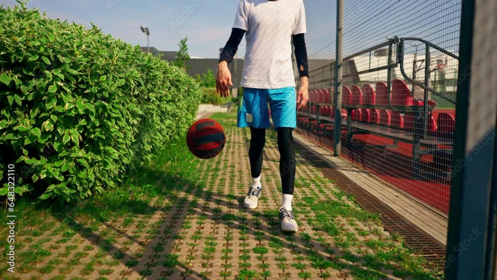 A tall guy basketball player walks down the park path to the basketball ...