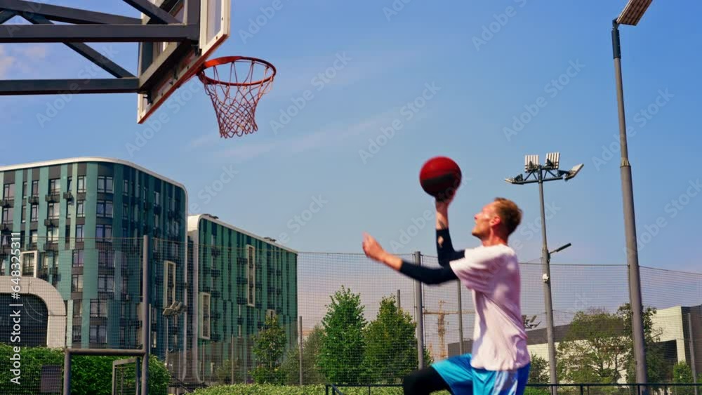 A tall guy basketball player throws a ball into a basketball hoop at a ...