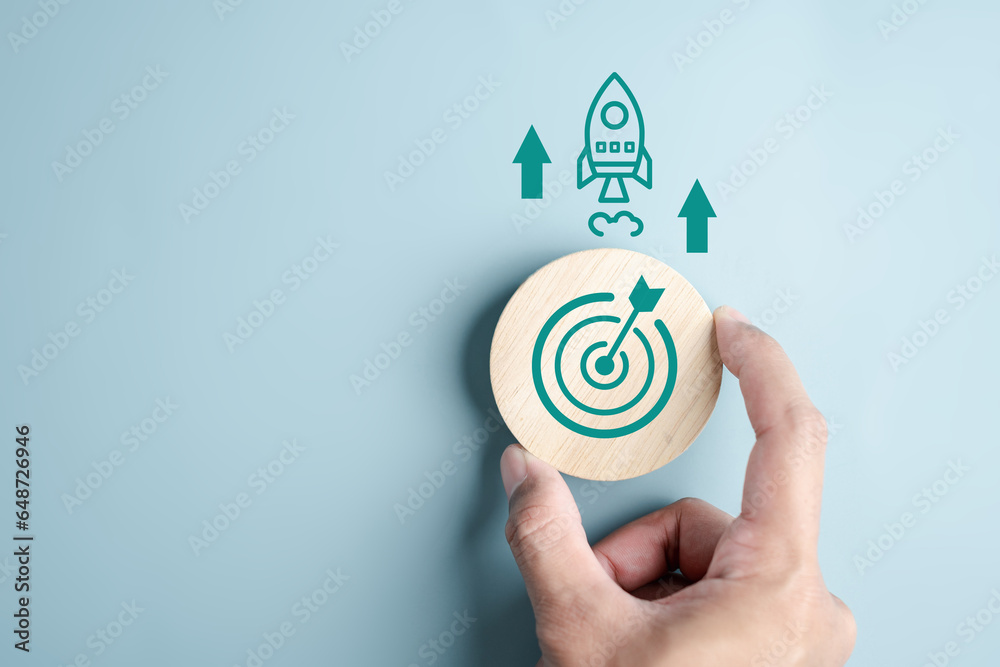 Hand holding objective aiming target and rocket ship launch arrow up to ...
