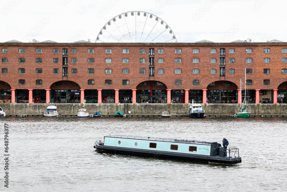 Boat passes the sight of the iconic Royal Albert Dock with the wheel of ...