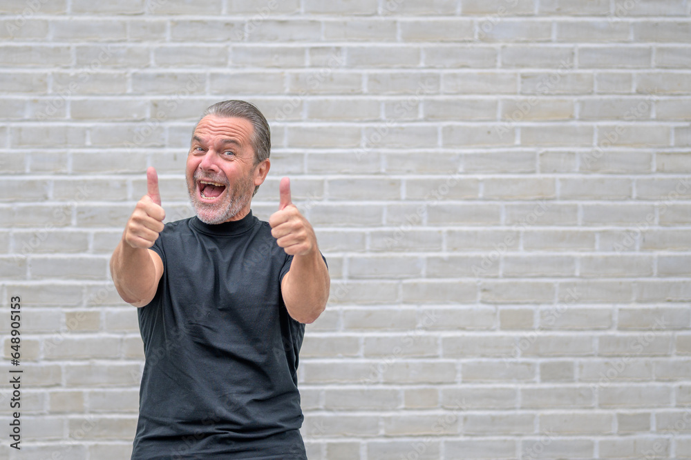 Man giving a double thumbs up gesture in front of a white brick wall ...